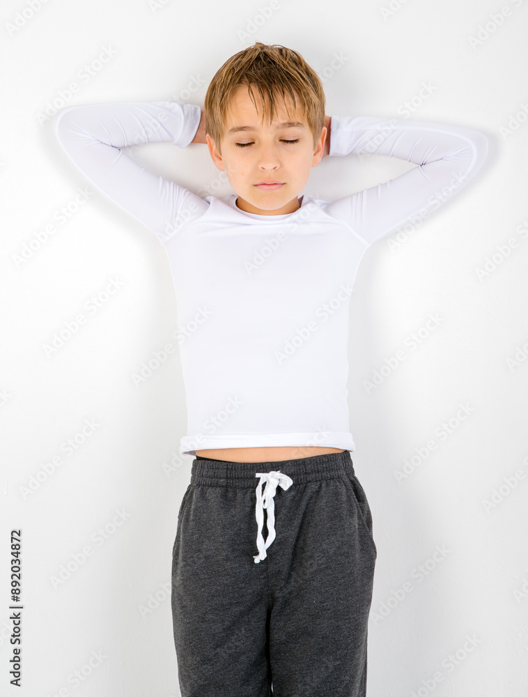 Young preteen boy with eyes closed standing against white studio wall ...