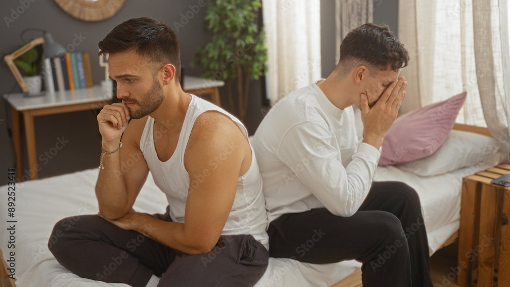 Two men looking distressed while sitting on a bed back-to-back in a ...