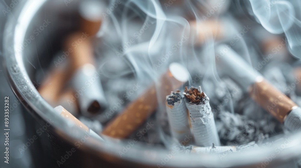 Ashtray densely filled with cigarette butts emitting smoke, symbolic of ...
