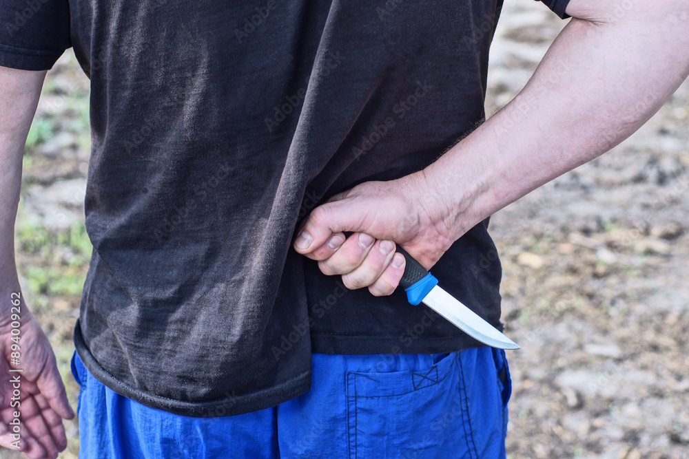 hand of a male criminal in black clothes and a gray knife behind his ...