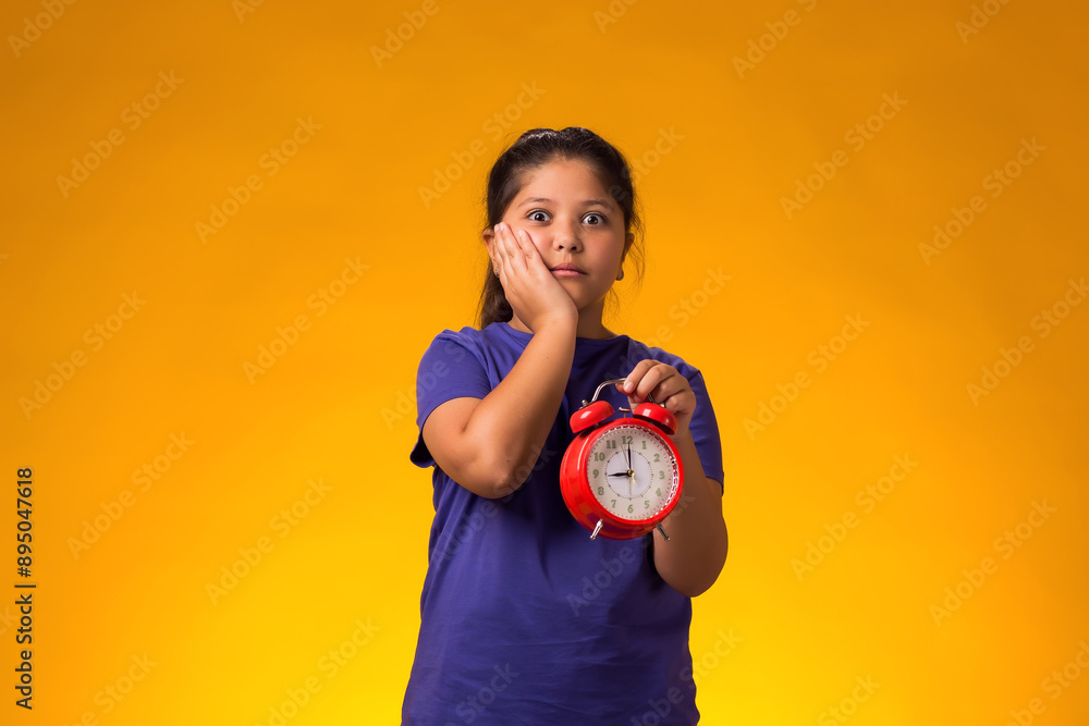 Surprised kid girl holding an alarm clock in hand. The concept of ...