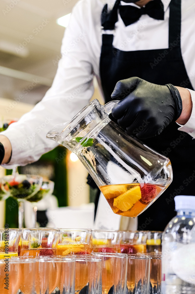 Bartender Pouring Fresh Fruit Cocktail in Glasses. Bartender in black gloves and apron pouring ...