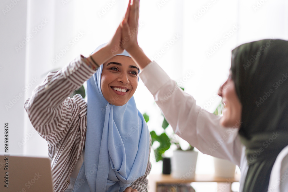 Three women in hijabs high-five each other in a modern office They are ...
