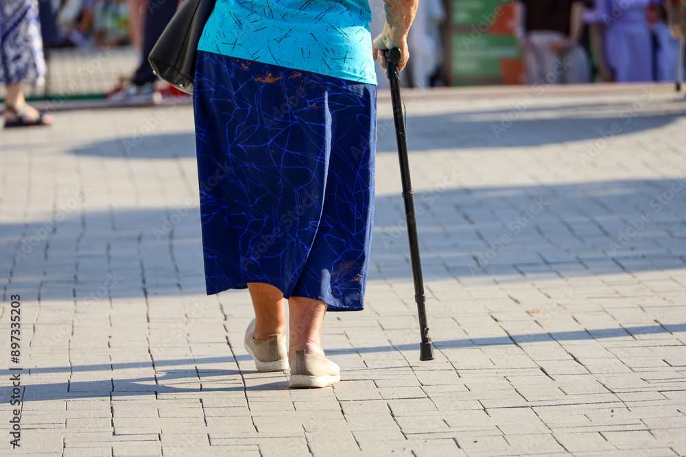 Elderly woman walking with cane on city street, legs on sidewalk ...