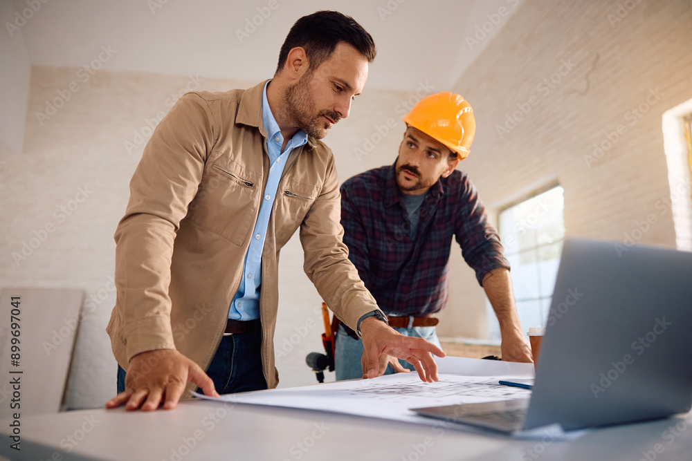 Mid adult man and construction worker examining housing plans during ...