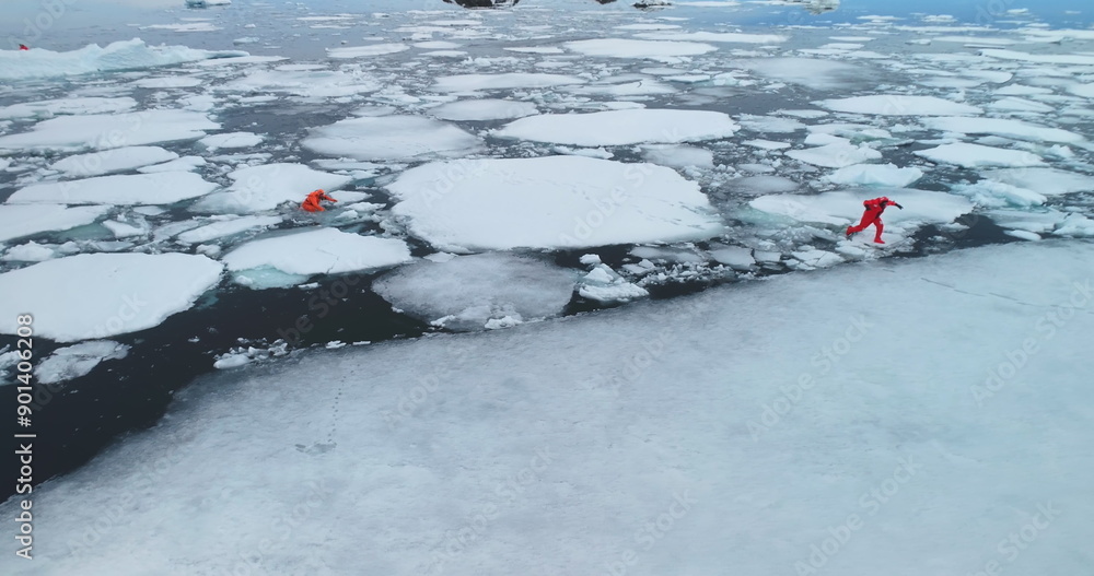 People in Antarctica ocean frozen ice floes. Two man in orange ...