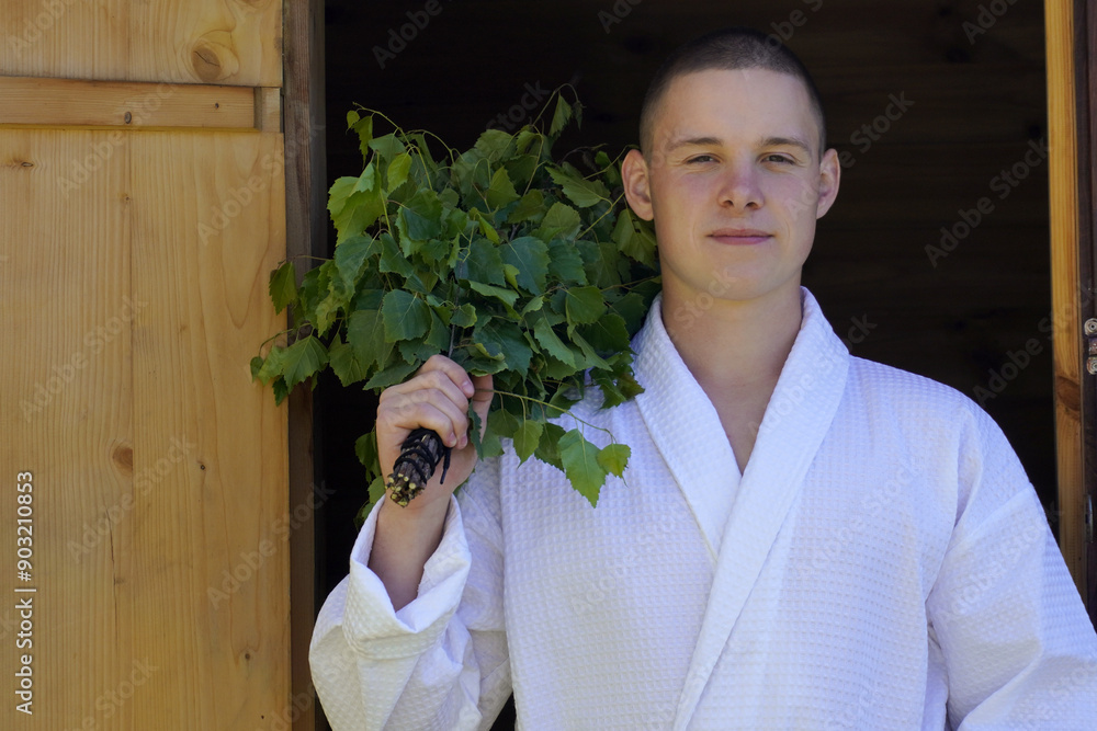20-year-old Caucasian guy with a fresh birch broom in the dressing room ...
