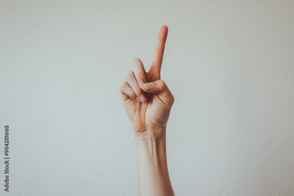 A hand is raised with one finger pointing upwards against a plain ...