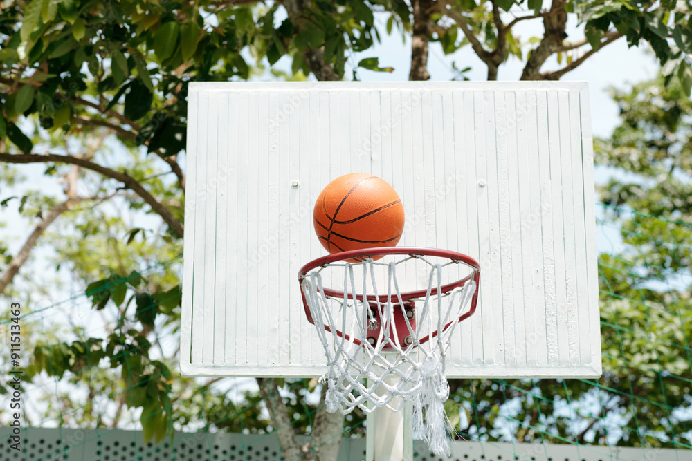 Basketball hoop mounted on backboard in outdoor setting, with ball mid ...