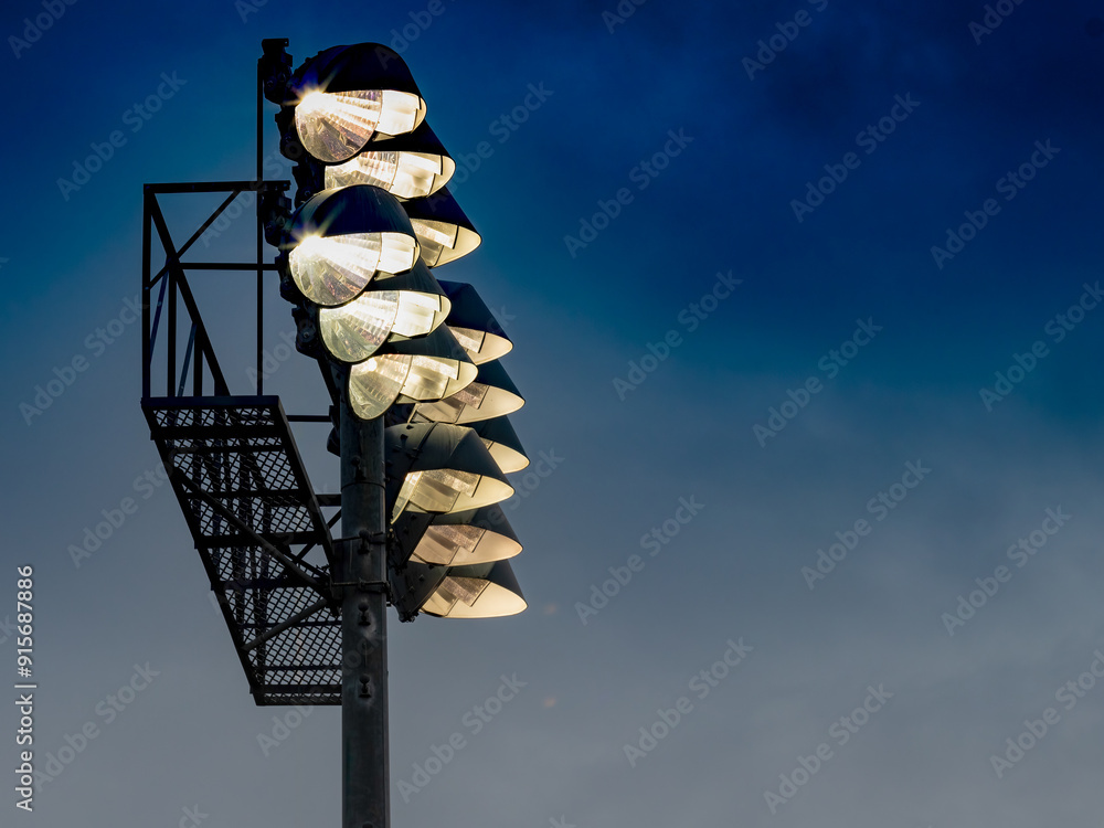 Illuminated stadium lights in a football stadium at dusk with a catwalk ...