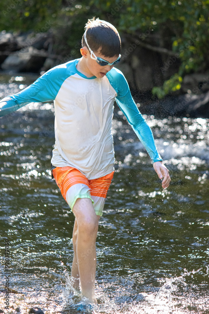 Boy wading through a creek after tubing, wearing swimwear and goggles ...