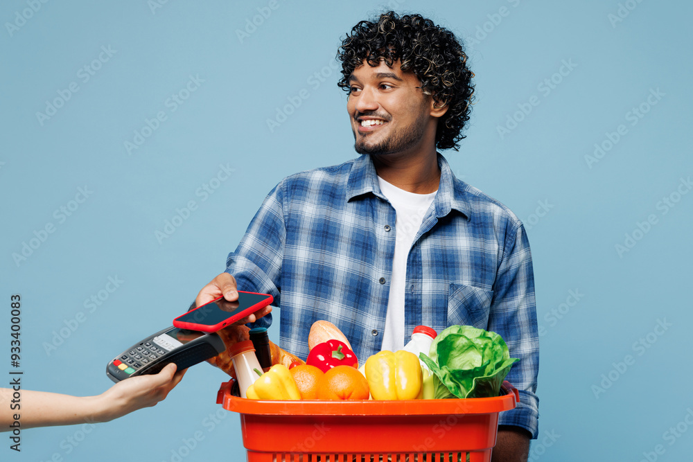 Young smiling happy Indian man he wear shirt hold red basket with food ...