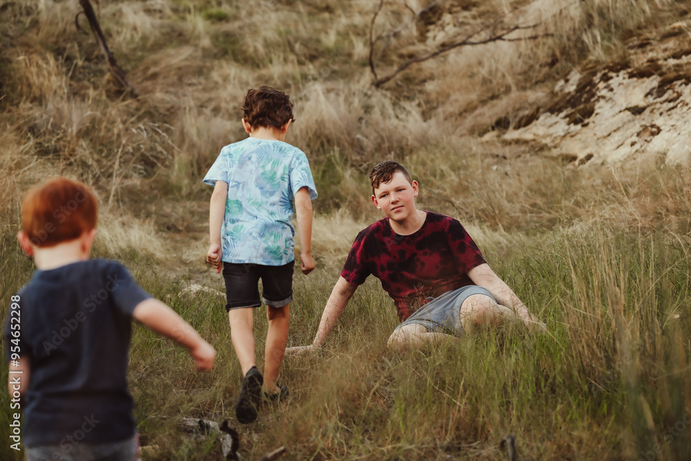 Big brother sitting on grass in the Australian bush with siblings ...