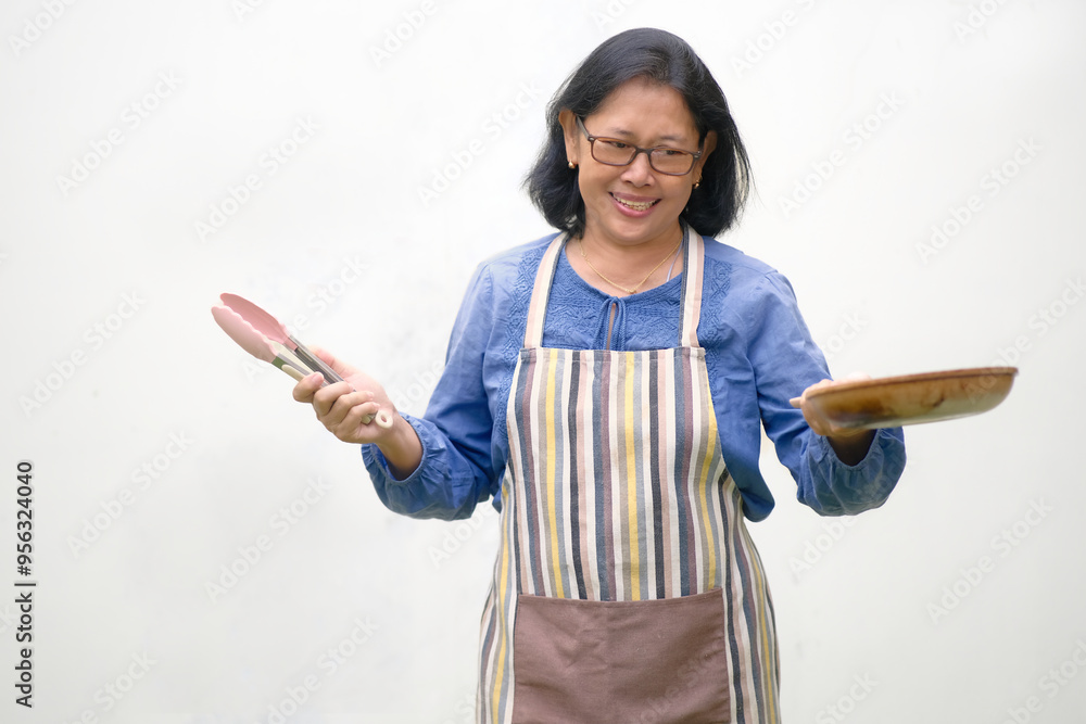 Facial expression of a housewife, standing and holding cooking utensils ...