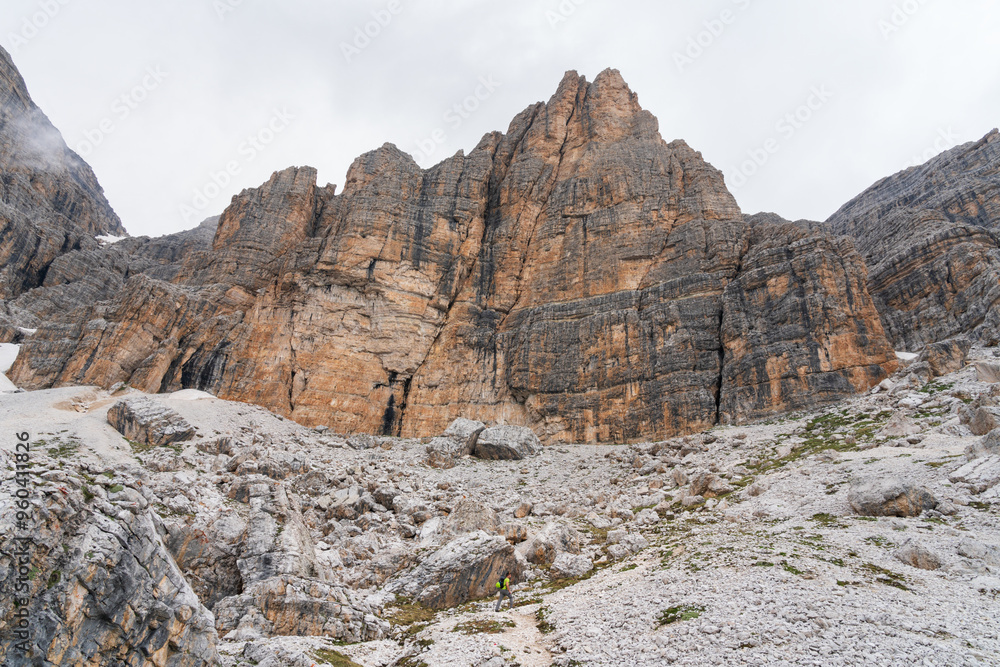 Vertical rocky mountain peak of Sella Group on a cloudy day. Climber ...