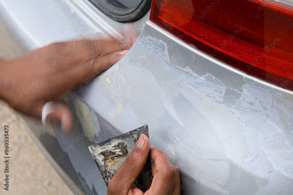 Repairing a scratched car bumper with a putty knife in a residential ...