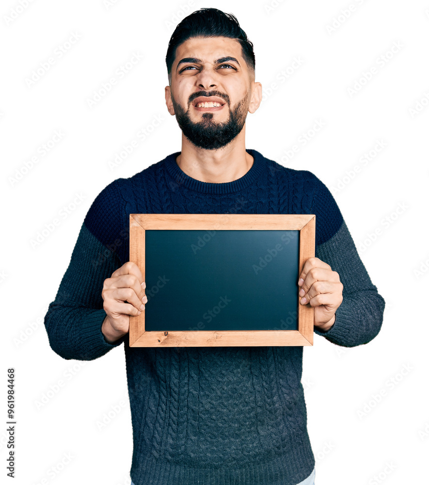 Young arab man with beard holding blackboard angry and mad screaming ...