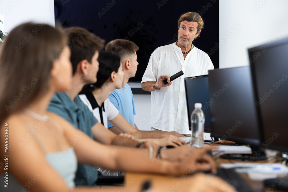 Positive adult male teacher guiding group of interested young people ...