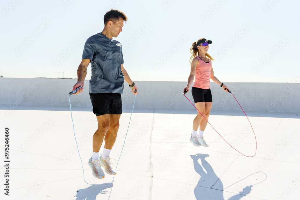 A man and woman jump rope in unison on a bright, sunny day, their ...
