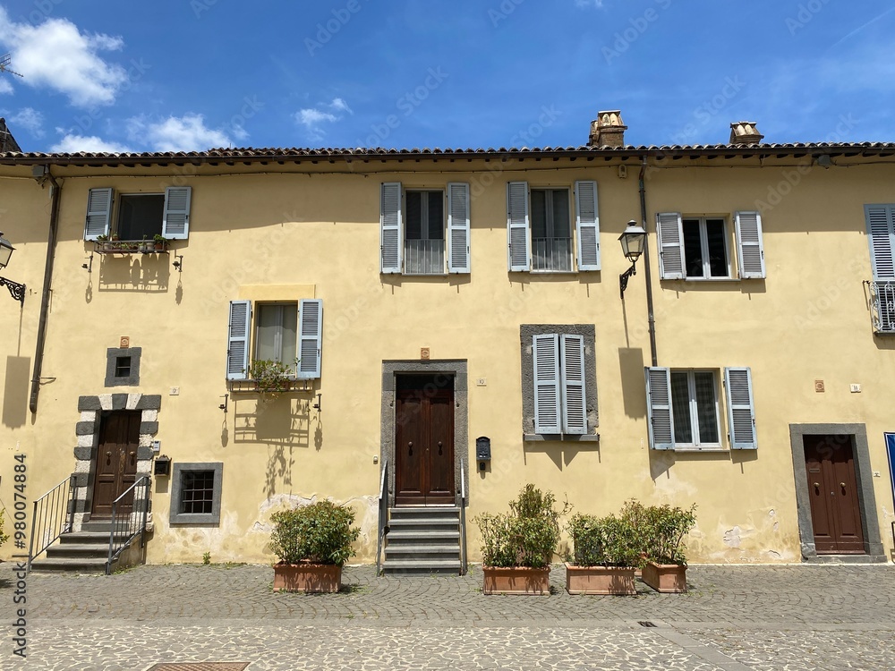 Charming Italian townhouse with pale yellow facade, blue shuttered ...