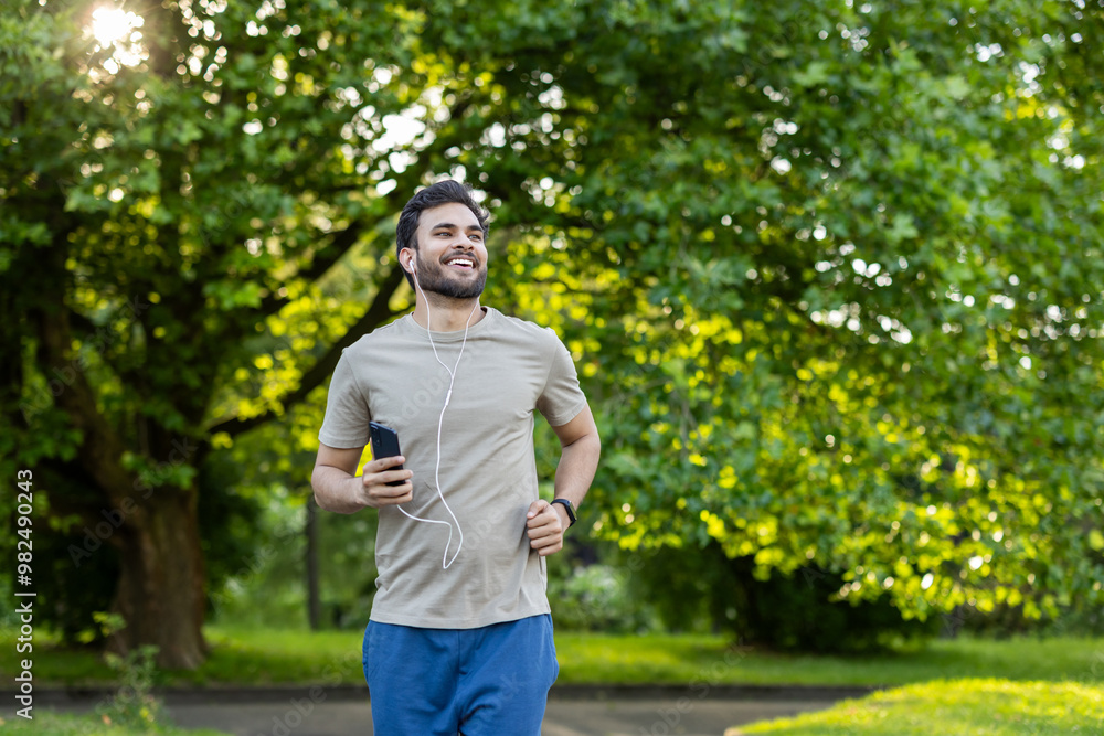 Active man jogging in lush green park with phone and headphones ...