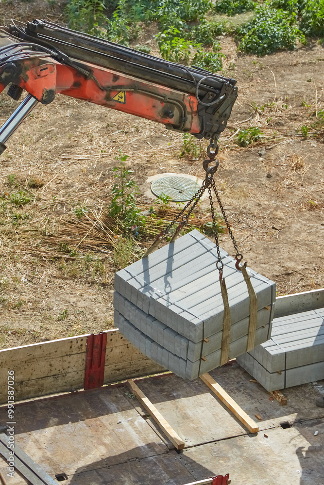 A loader crane unloads concrete garden barriers from the truck bed ...