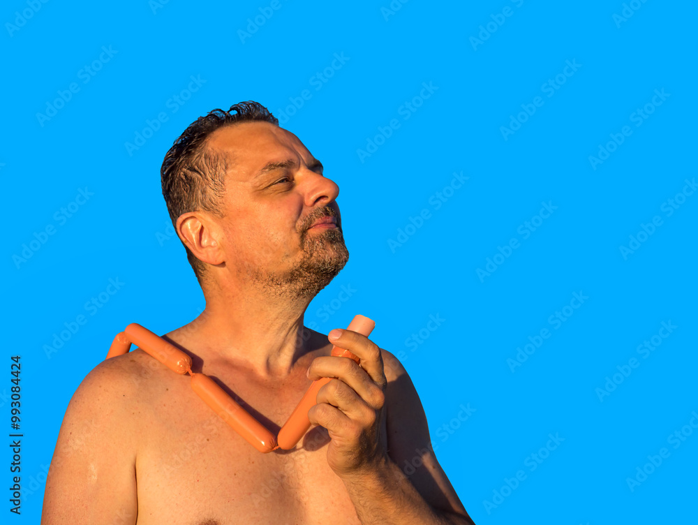 Sad mature man topless posing with barbecue sausages on against blue ...