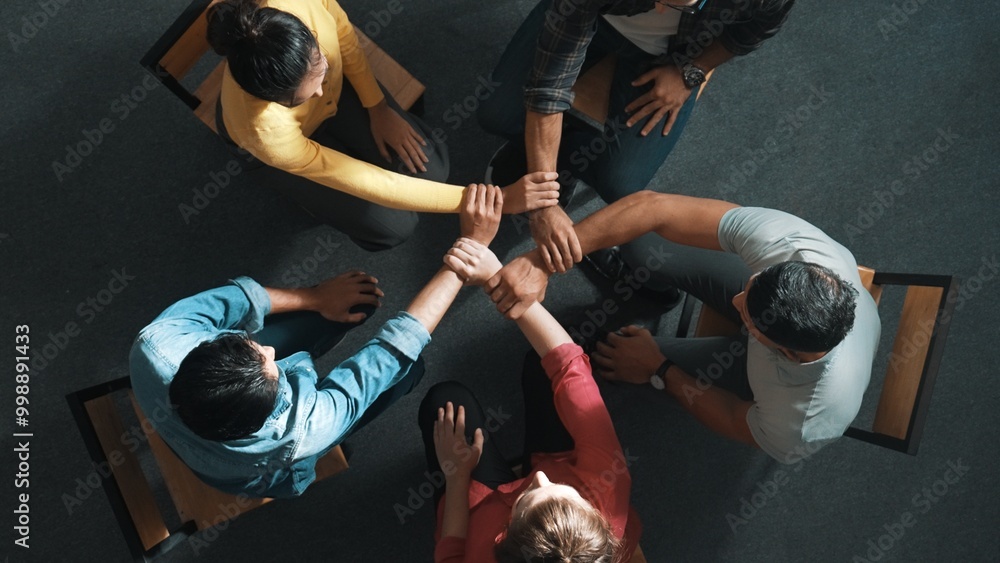 Top down aerial view of diverse business people hold wrist while sitting circle together ...