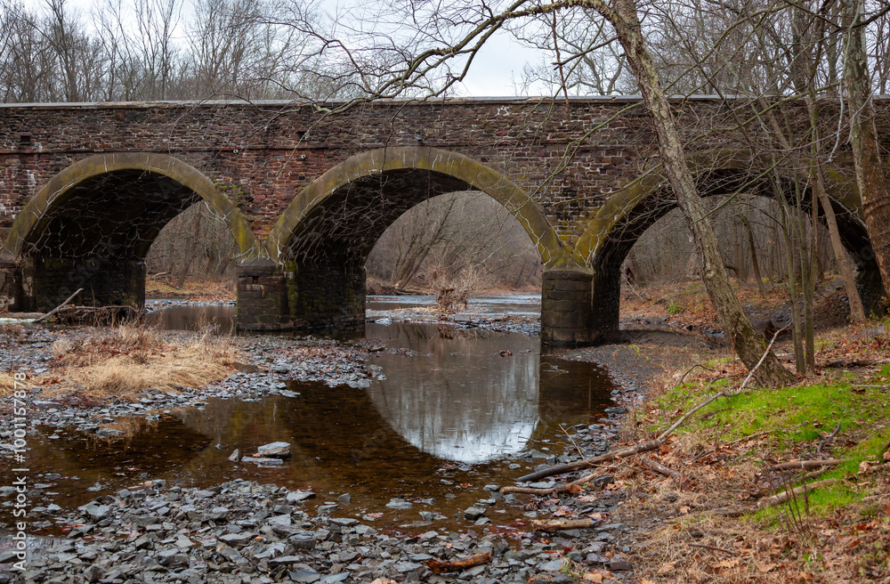 An ancient moss-covered stone arch bridge crosses a quiet river ...