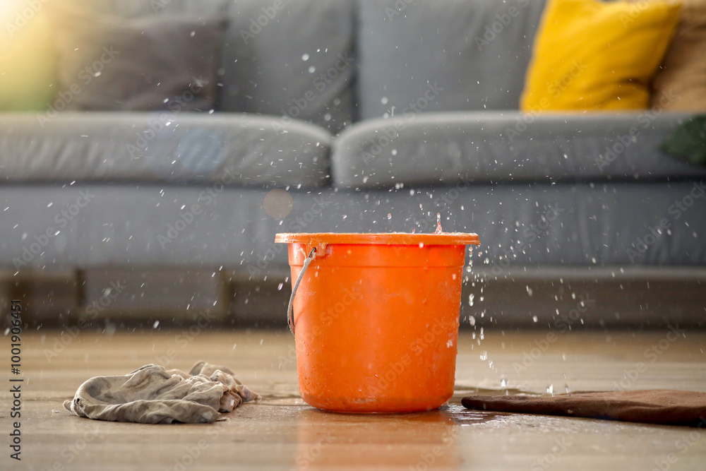 Water dripping from ceiling into plastic bucket on floor in living room ...