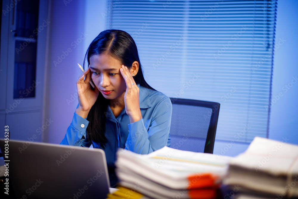 Asian businesswoman works late into the night in her office, documents ...