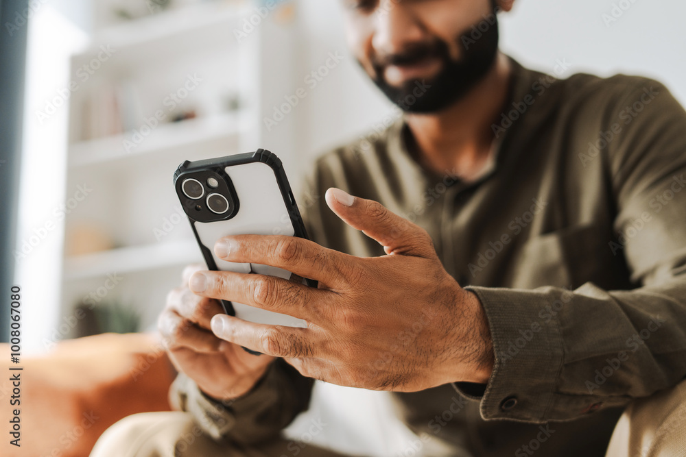 Young man smiling while holding mobile phone, using mobile app at home ...