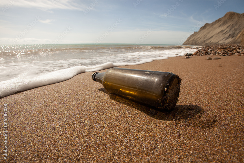 Used glass water bottle washed up on the shore of a beach, highlighting ...