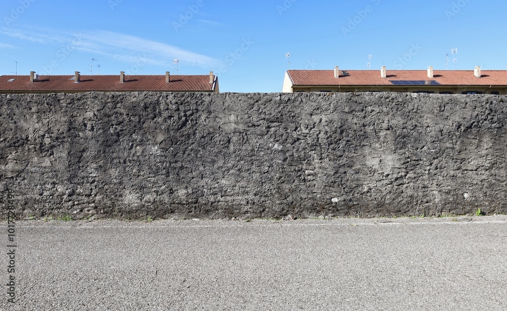 Rough concrete surrounding wall with two rooftops with chimneys and ...