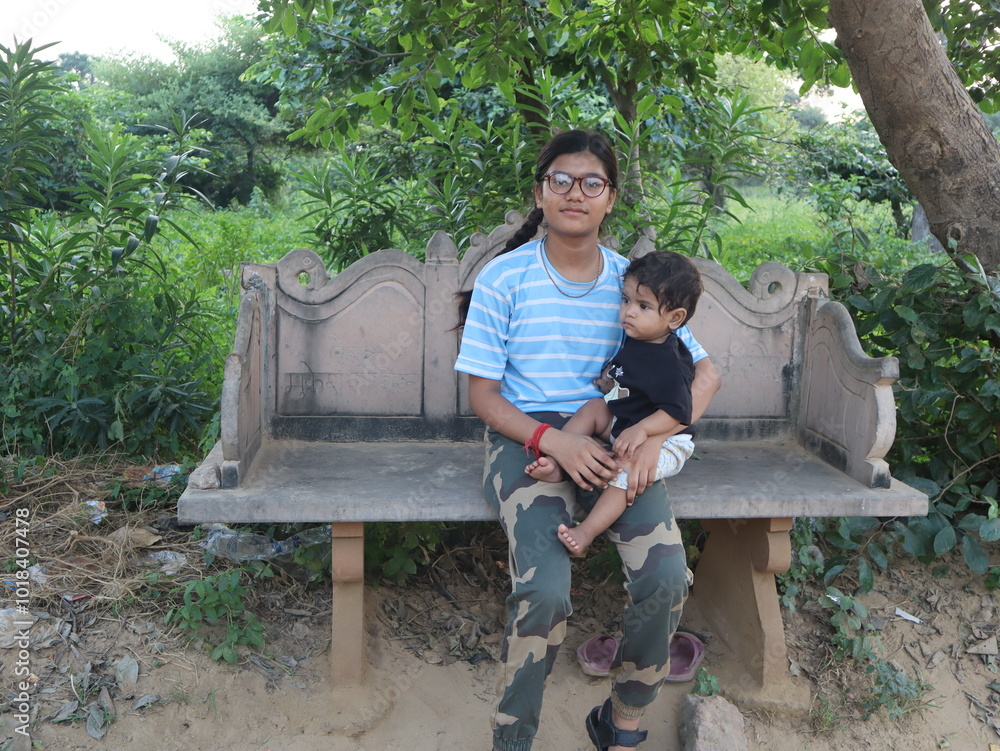 A teenage sister sits with his 1-year-old baby sister on a cement seat ...