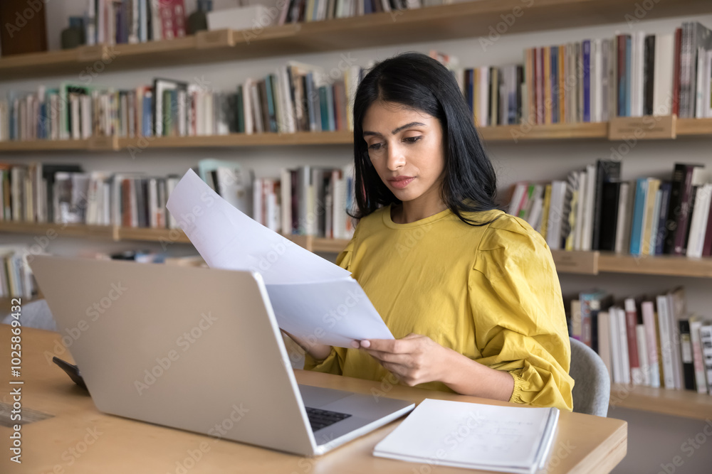 Serious Indian student working on research paper in library, reading ...