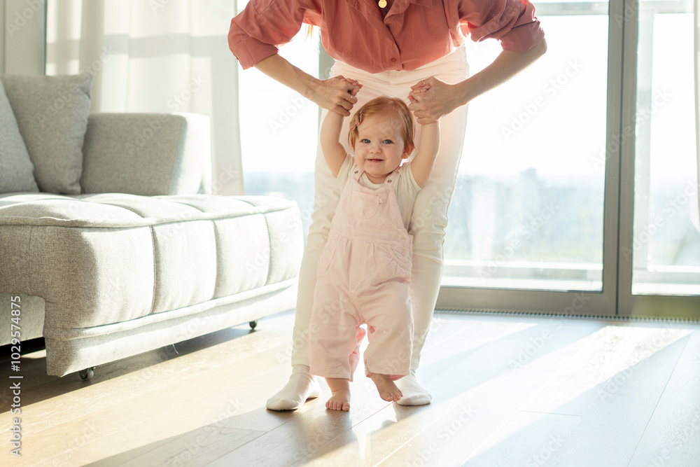 Baby girl taking first steps with mother's help at home, walking on ...