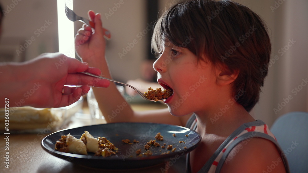 Reluctant young boy being fed by a parent, initially hesitating but ...