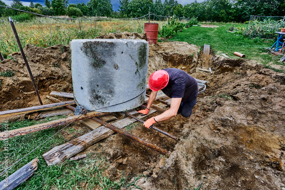 Worker moves heavy concrete ring using roller deck made of steel pipes ...