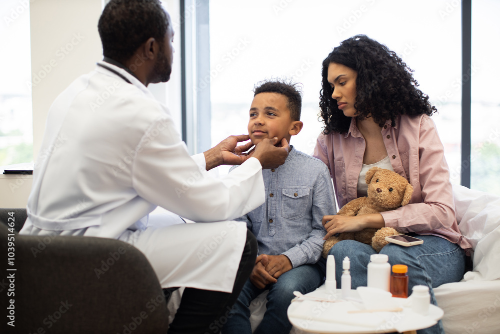 African doctor examines young African boy's lymph nodes while seated by ...
