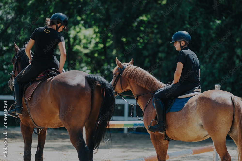 Two equestrians participate in an outdoor riding lesson. Both wear ...