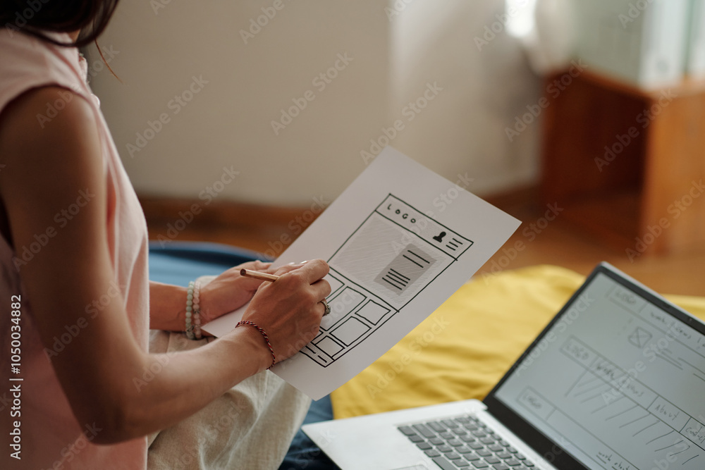 Person sketching website layout on paper while referencing design on ...