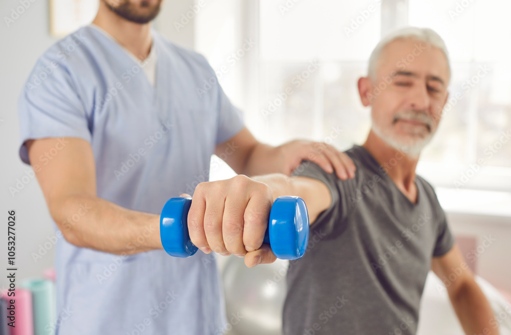 Professional physiotherapist at gym helps old aged man do exercises for arm, shoulder and elbow ...