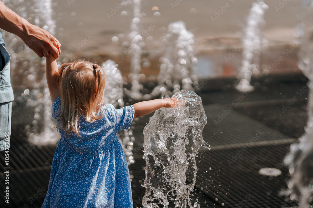 Caucasian cute child toddler girl in a dress playing with fountains ...