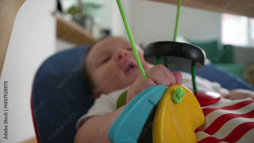 Baby reaching up and playing with colorful hanging toys while lying in ...