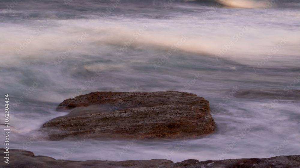Slow shutter speed photo of ocean water flowing over a rock, located at ...