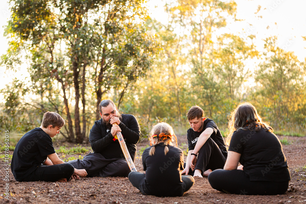 First Nations Australian man with his kids sitting in bushland playing ...