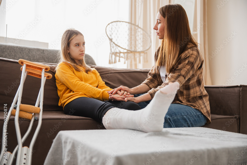 Girl with broken leg in cast sits with mother on couch at home. Sad ...