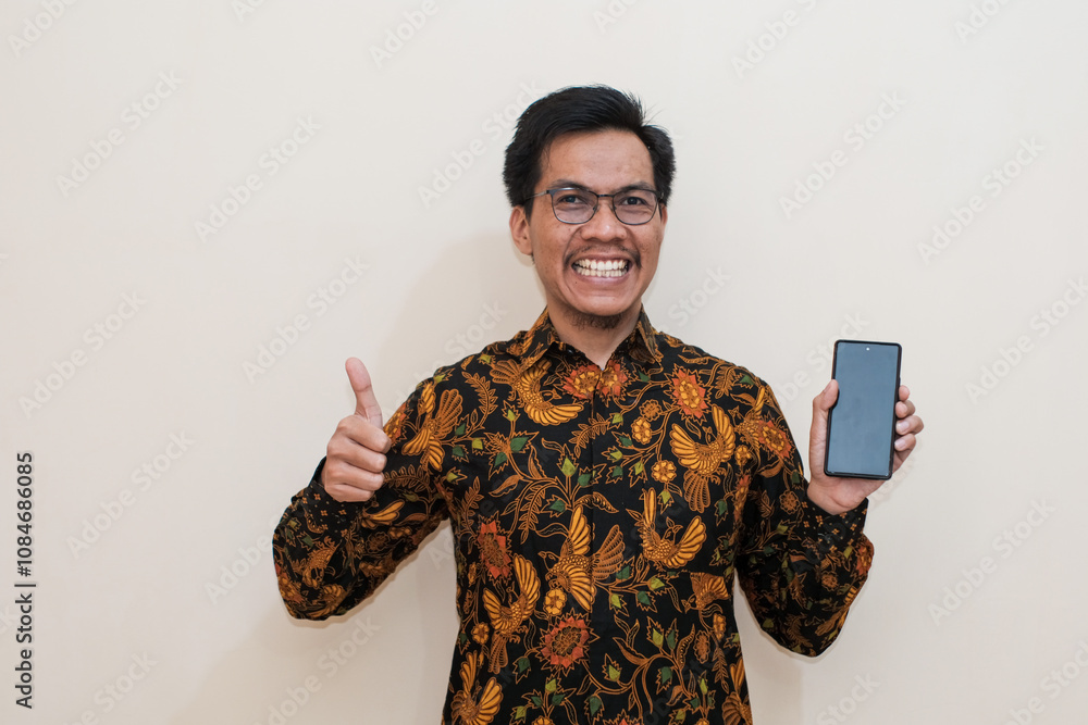 Southeast Asian man wearing batik shirt and glasses showing smartphone ...