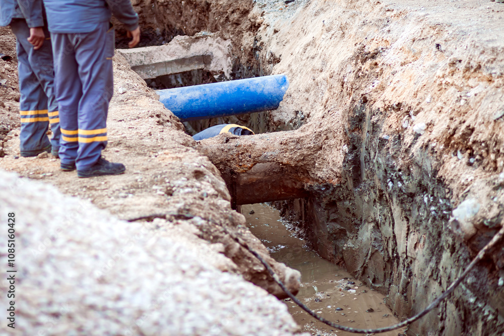 Construction workers inspecting a trench with muddy water and a large ...